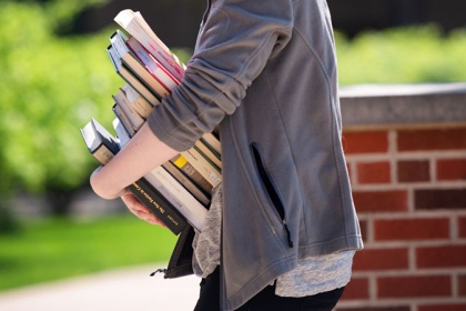 Student walking across campus, carrying multiple books.
