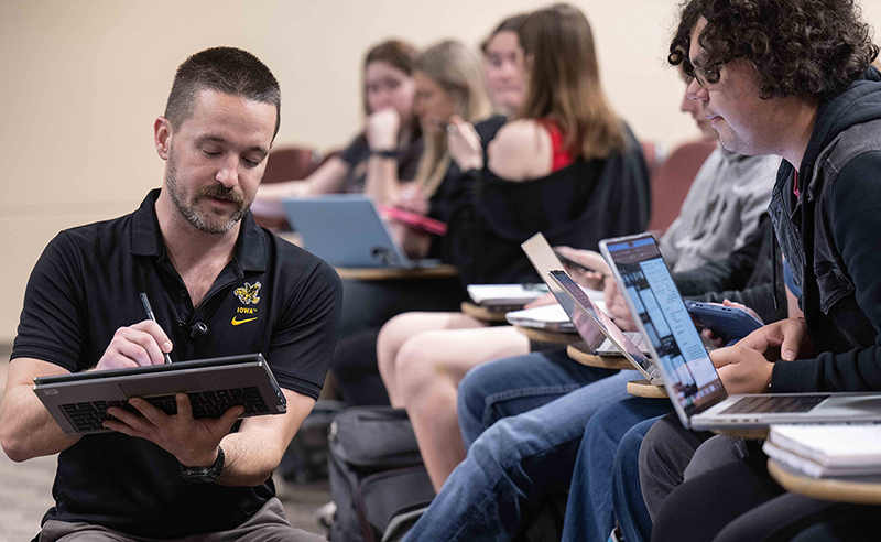 Adam Brummett demonstrates a concept to a student on a tablet in a ...